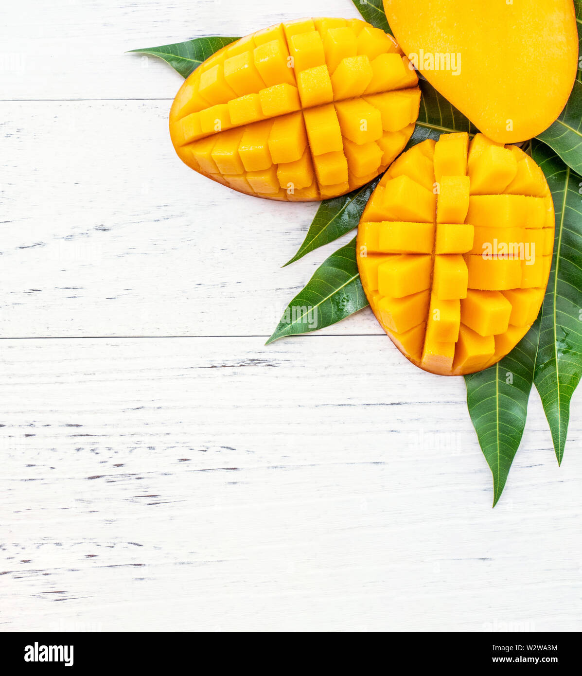 Beautiful chopped mango with green leaves on bright white color timber ...