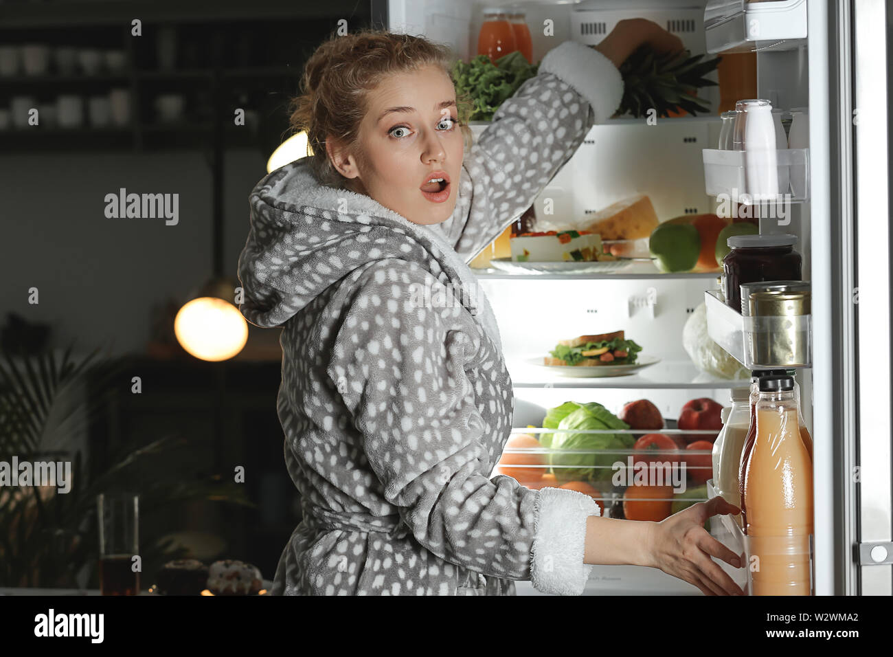 Afraid woman caught in the act of choosing tasty food in refrigerator ...