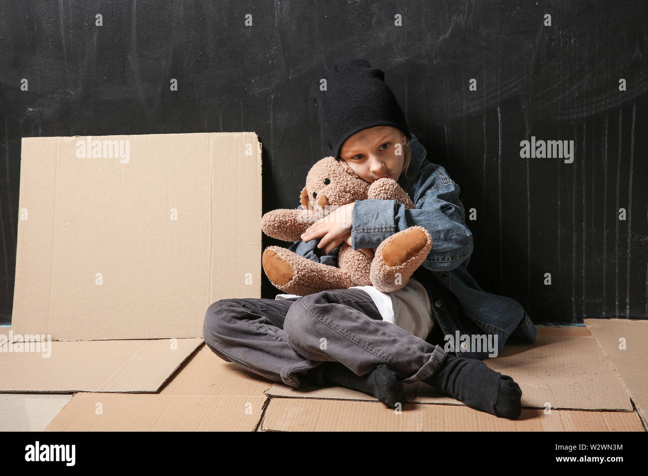 Homeless little girl with teddy bear sitting on floor near dark wall ...