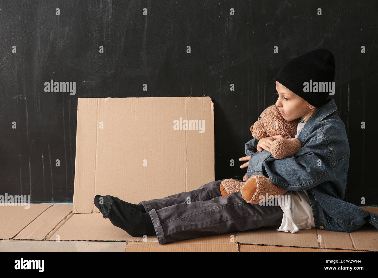 Homeless little girl with teddy bear sitting on floor near dark wall ...