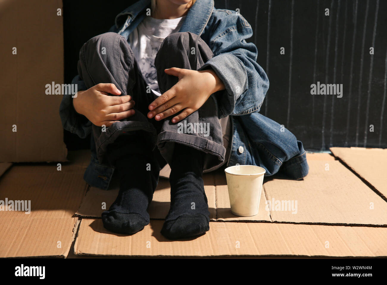 Homeless little girl sitting on floor near dark wall Stock Photo - Alamy