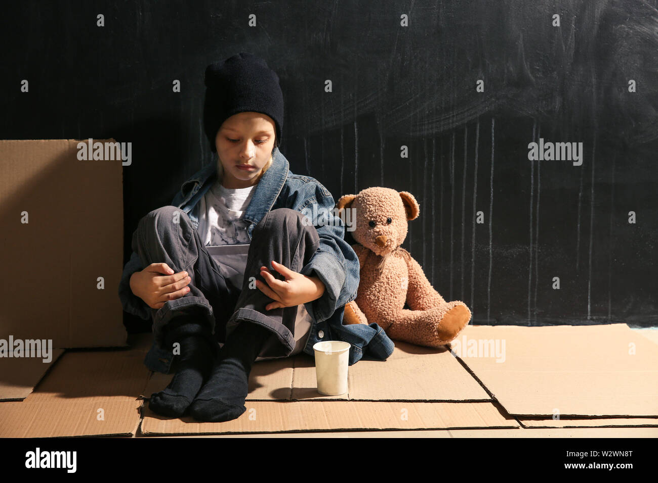 Homeless little girl sitting on floor near dark wall Stock Photo - Alamy
