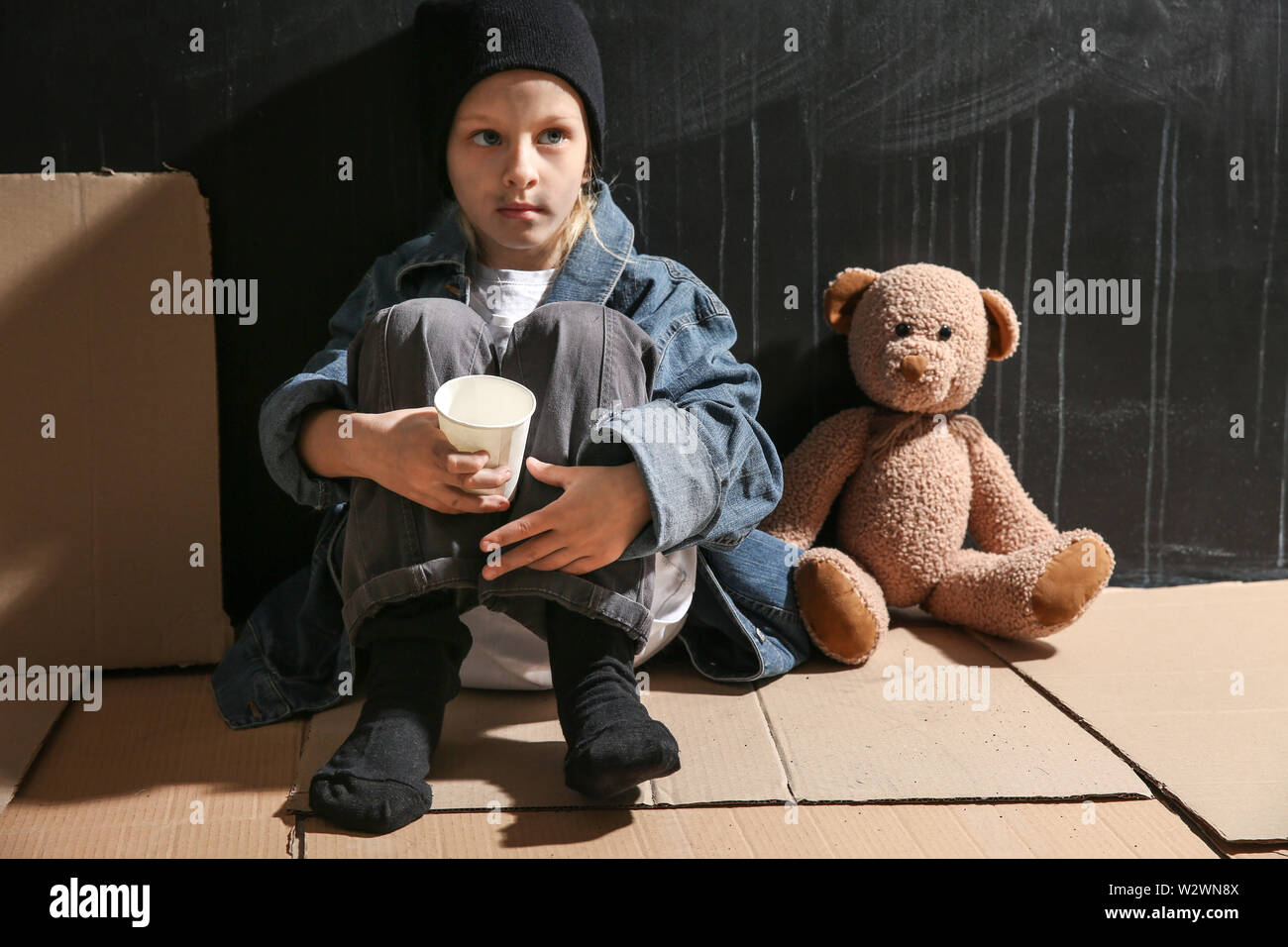 Homeless little girl sitting on floor near dark wall Stock Photo - Alamy