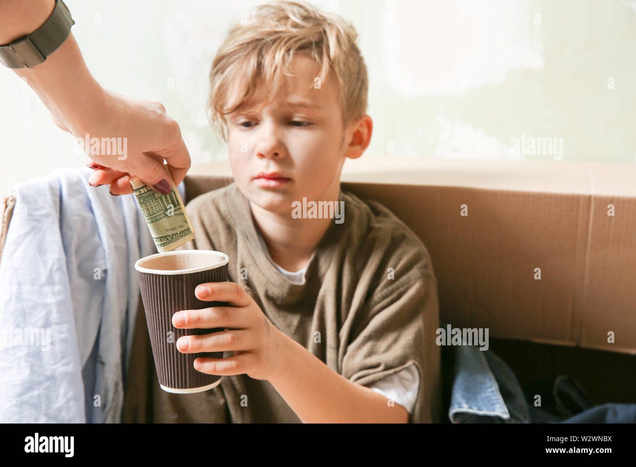 Woman giving money to homeless little boy indoors Stock Photo - Alamy