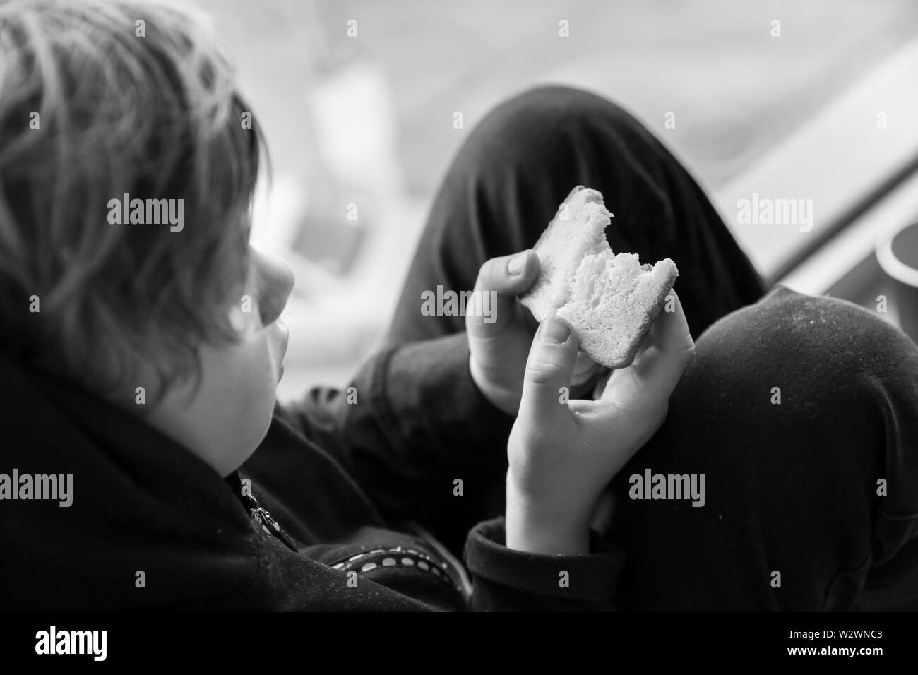 Homeless little boy with bread sitting on window sill indoors Stock ...