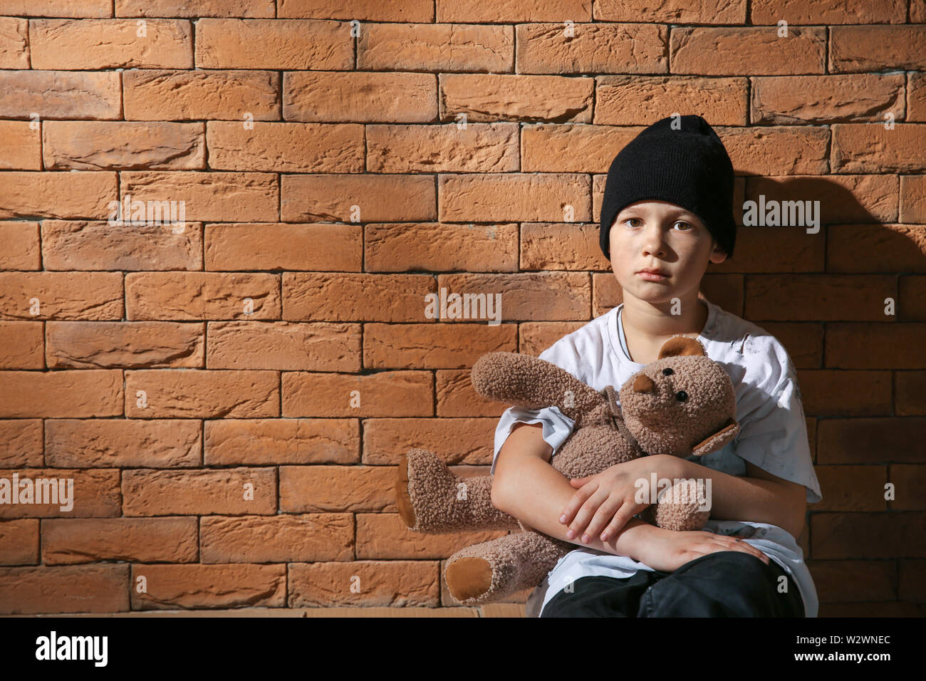 Homeless little boy with teddy bear sitting near brick wall Stock Photo ...