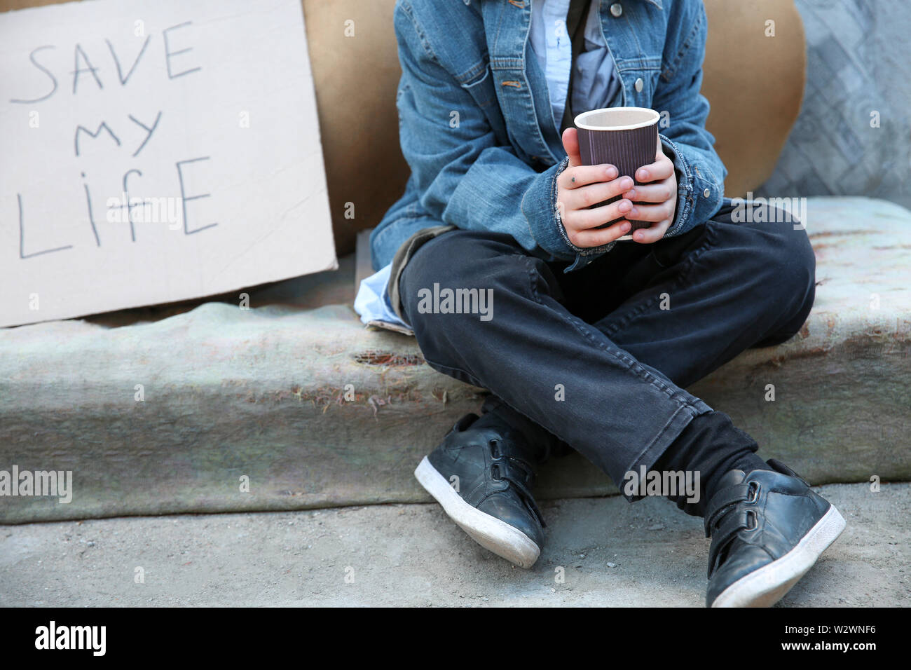 Homeless little boy with cup sitting outdoors Stock Photo - Alamy