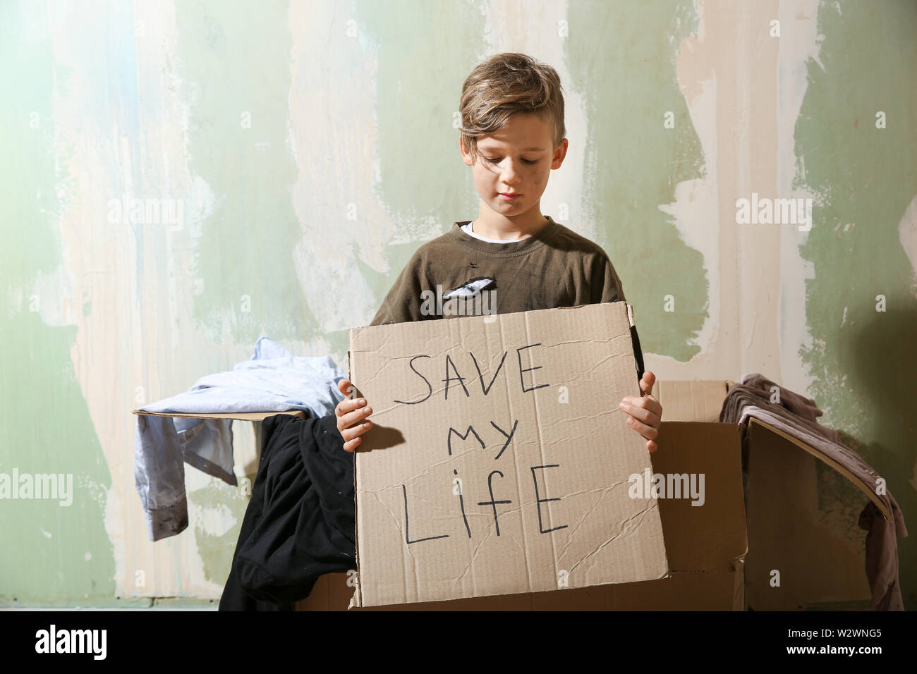 Homeless little boy holding piece of cardboard with text SAVE MY LIFE ...