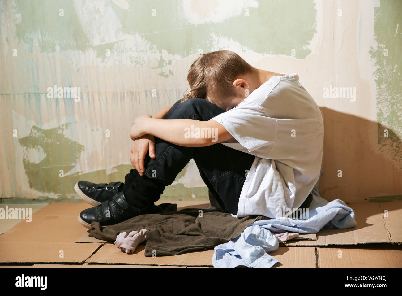 Homeless little boy sitting on floor near wall Stock Photo - Alamy