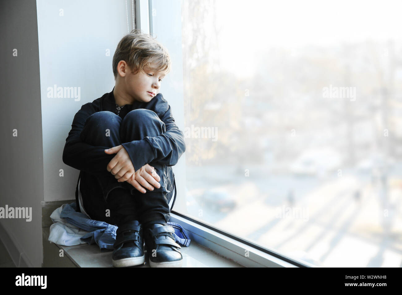 Homeless little boy sitting on window sill indoors Stock Photo - Alamy