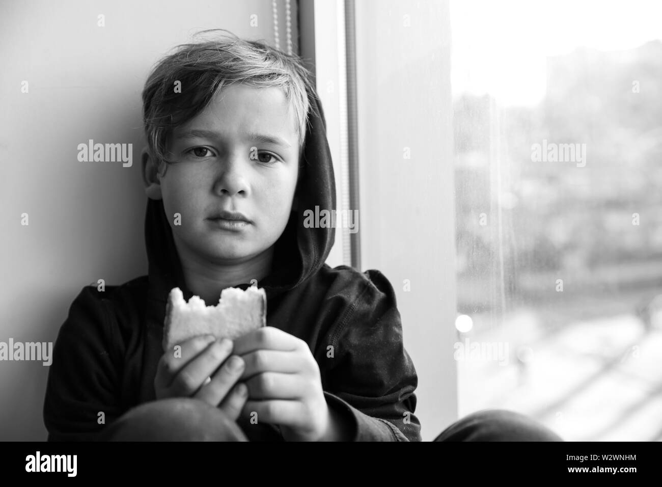 Homeless little boy with bread sitting on window sill indoors Stock ...