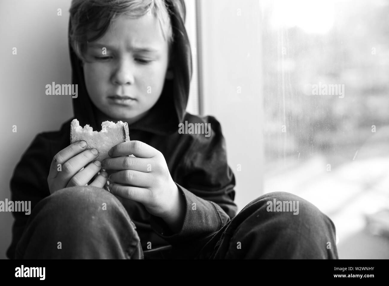 Homeless little boy with bread sitting on window sill indoors Stock ...
