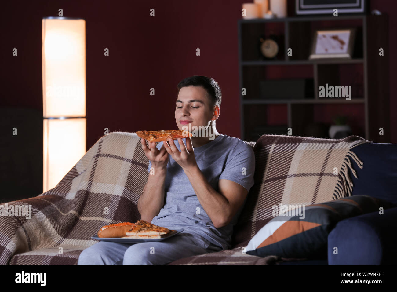 Handsome young man eating unhealthy food while watching TV at night ...