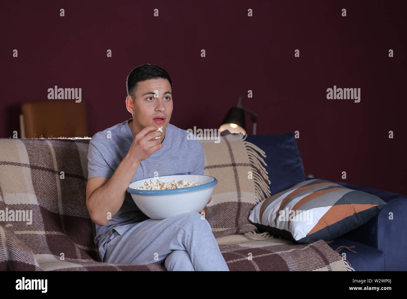 Handsome young man eating unhealthy food while watching TV at night ...