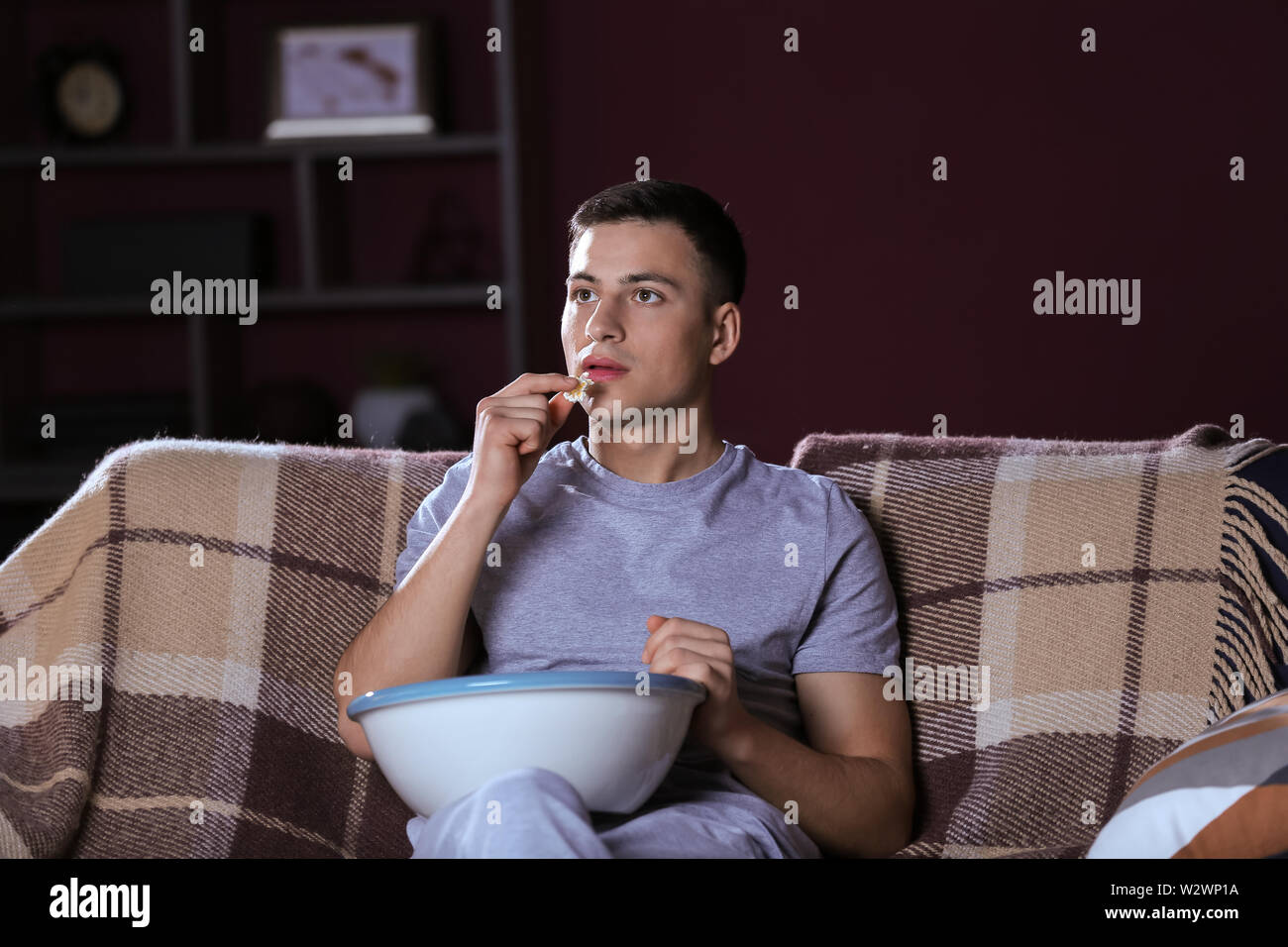 Handsome young man eating unhealthy food while watching TV at night ...