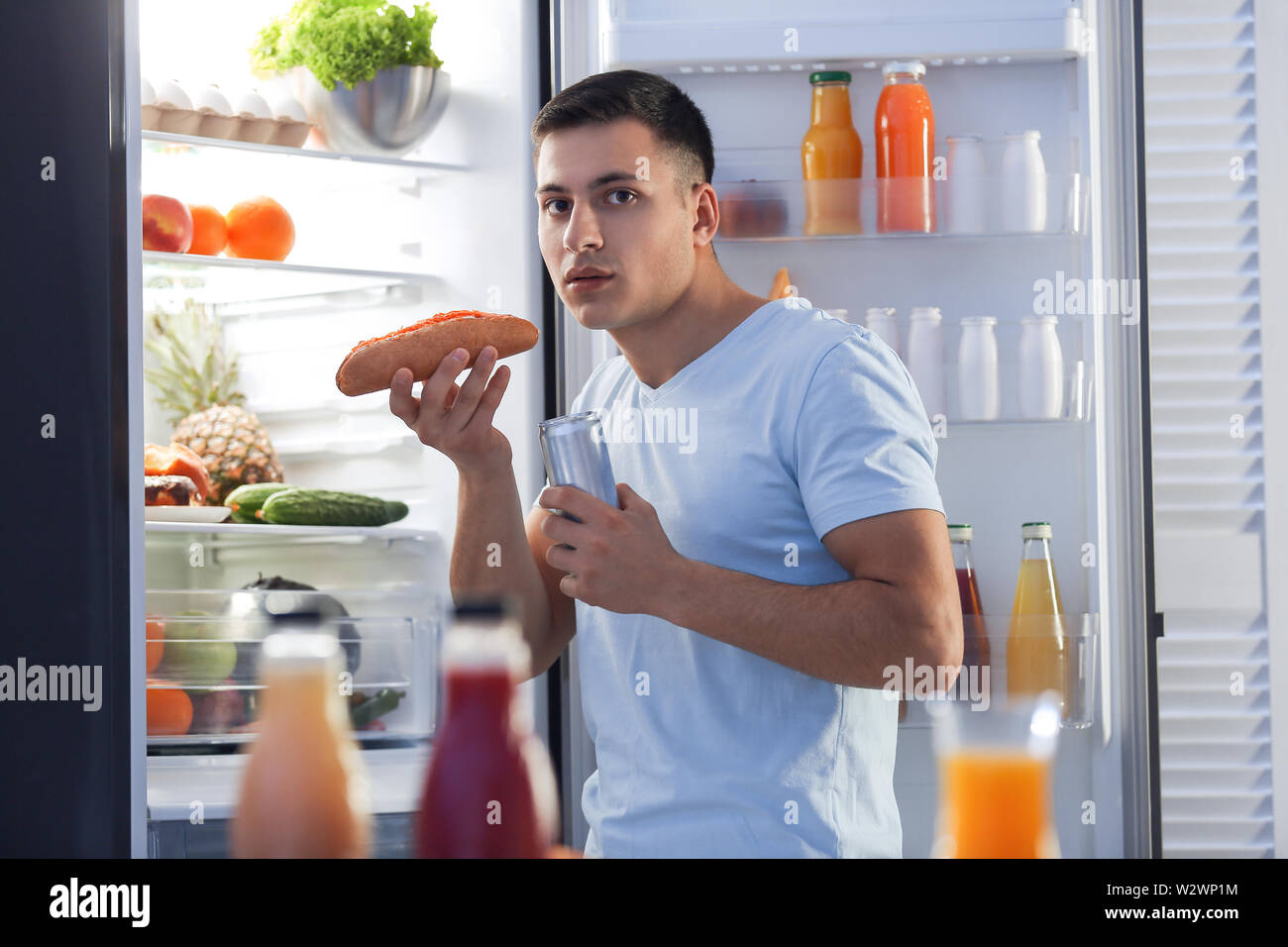 Afraid man caught in the act of eating unhealthy food near refrigerator ...