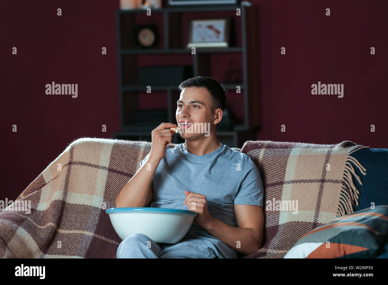Handsome young man eating unhealthy food while watching TV at night ...