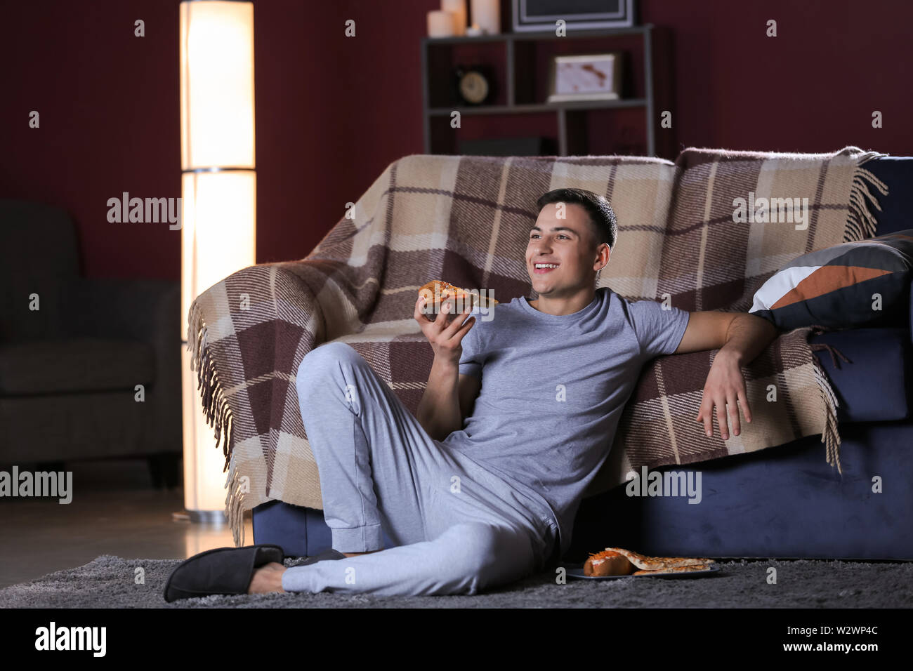 Handsome young man eating unhealthy food while watching TV at night ...