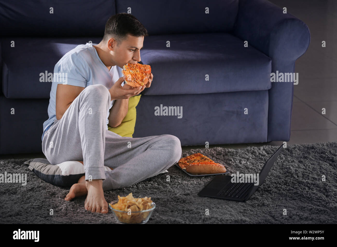 Handsome young man eating unhealthy food while watching movie at night ...