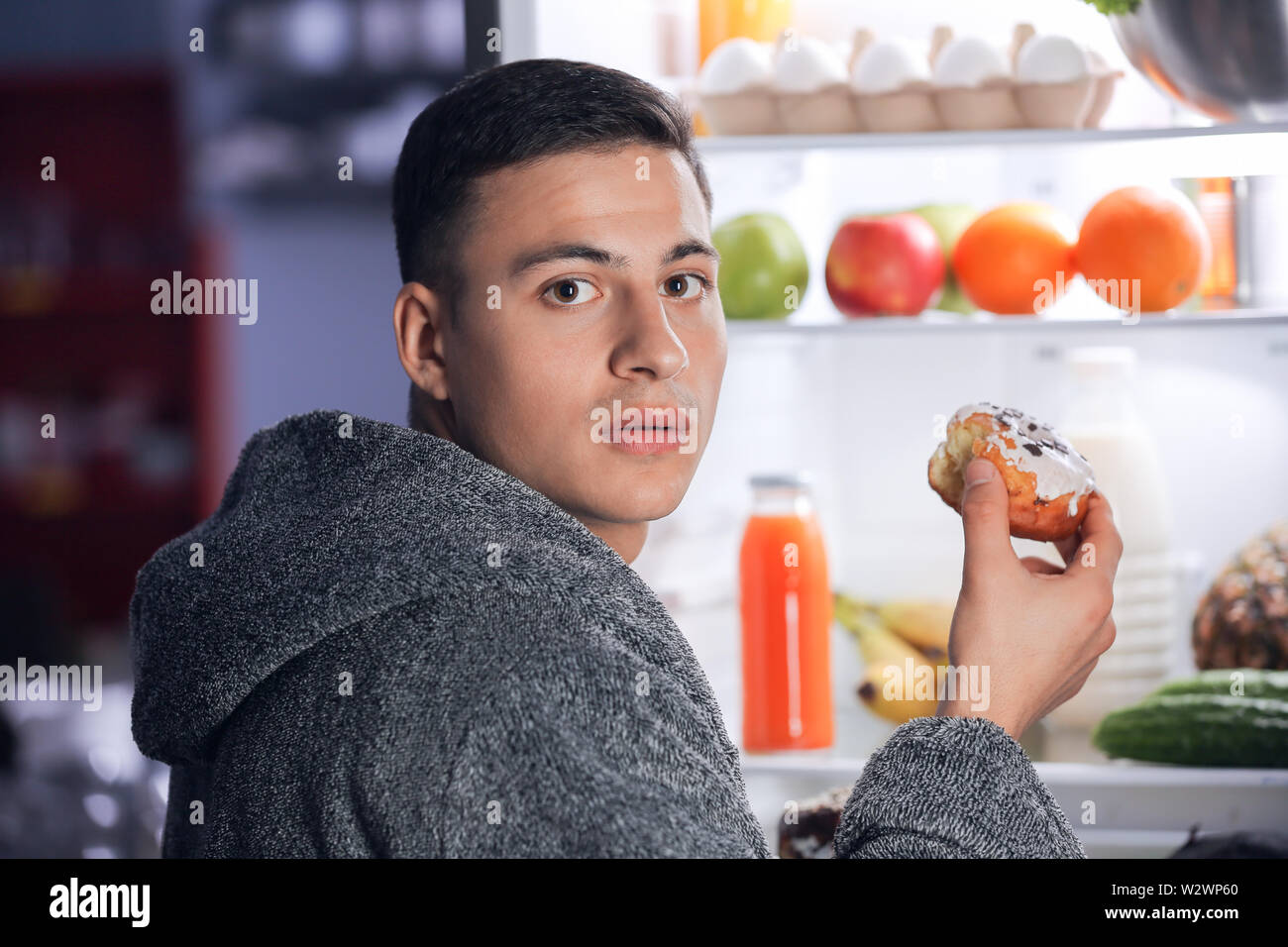 Afraid man caught in the act of eating unhealthy food near refrigerator ...