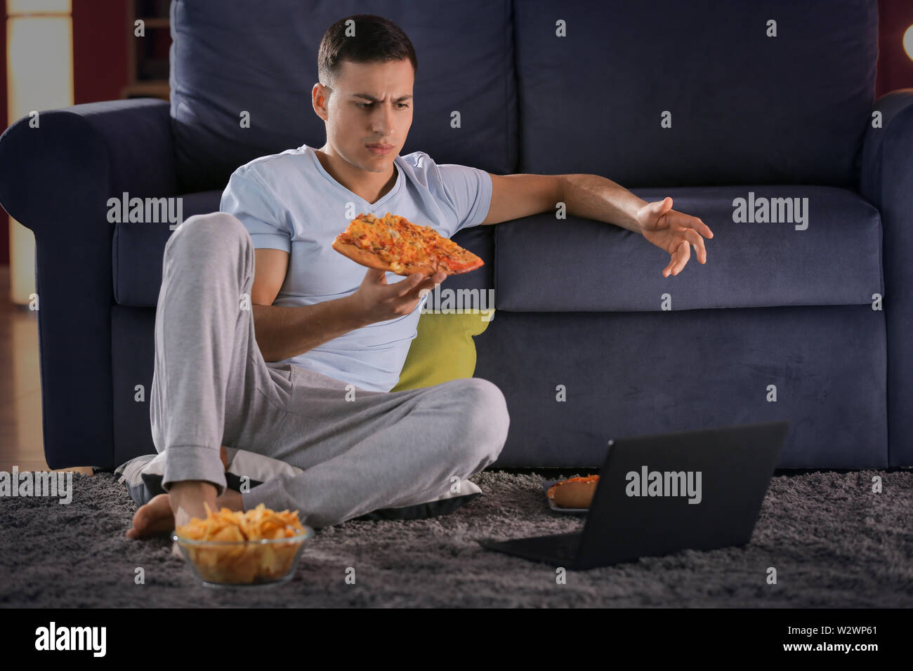 Handsome young man eating unhealthy food while watching movie at night ...