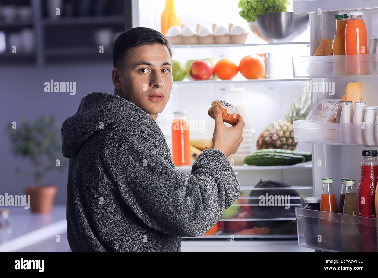 Afraid man caught in the act of eating unhealthy food near refrigerator ...