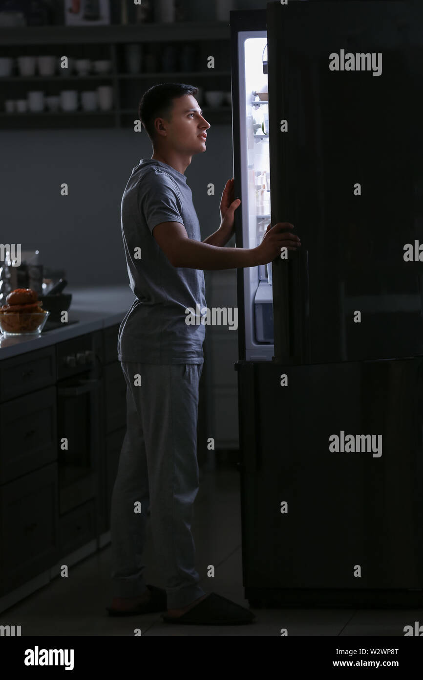 Handsome young man choosing food in refrigerator at night Stock Photo ...