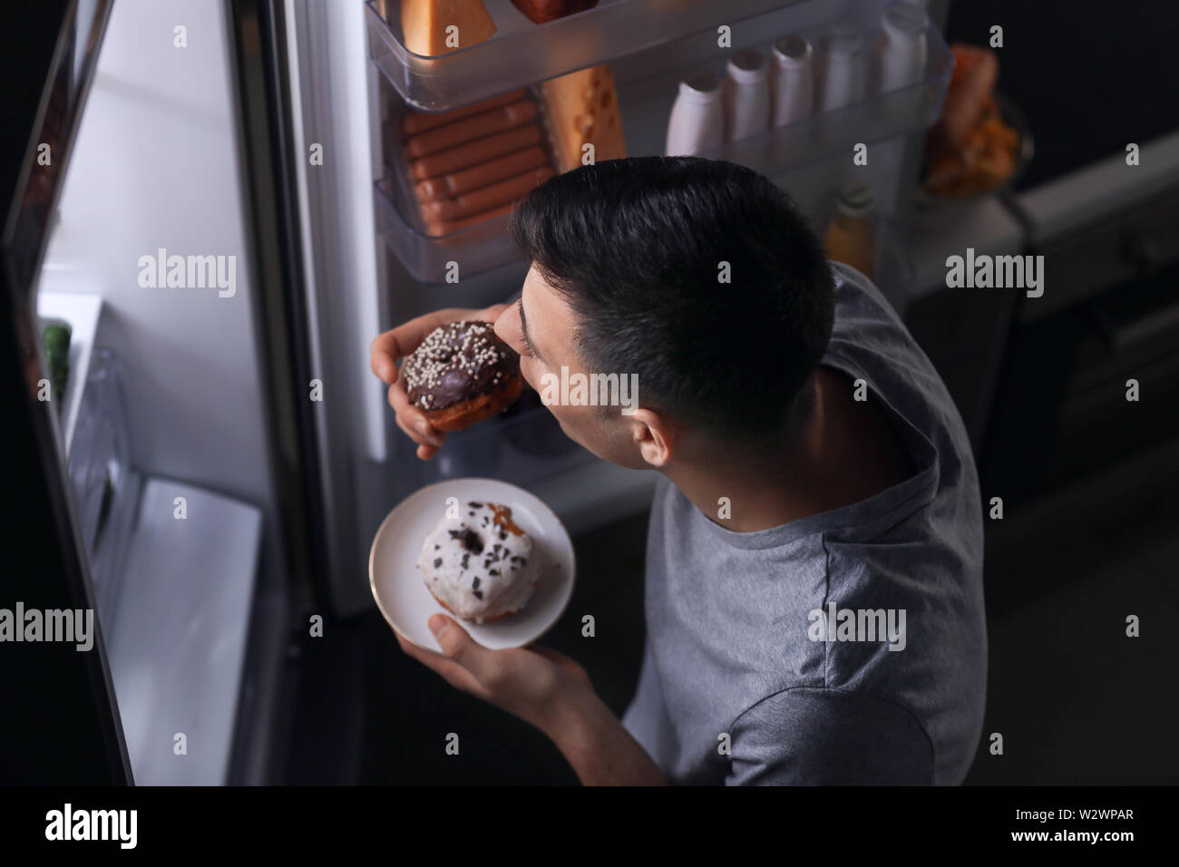 Young man eating food near refrigerator at night Stock Photo - Alamy