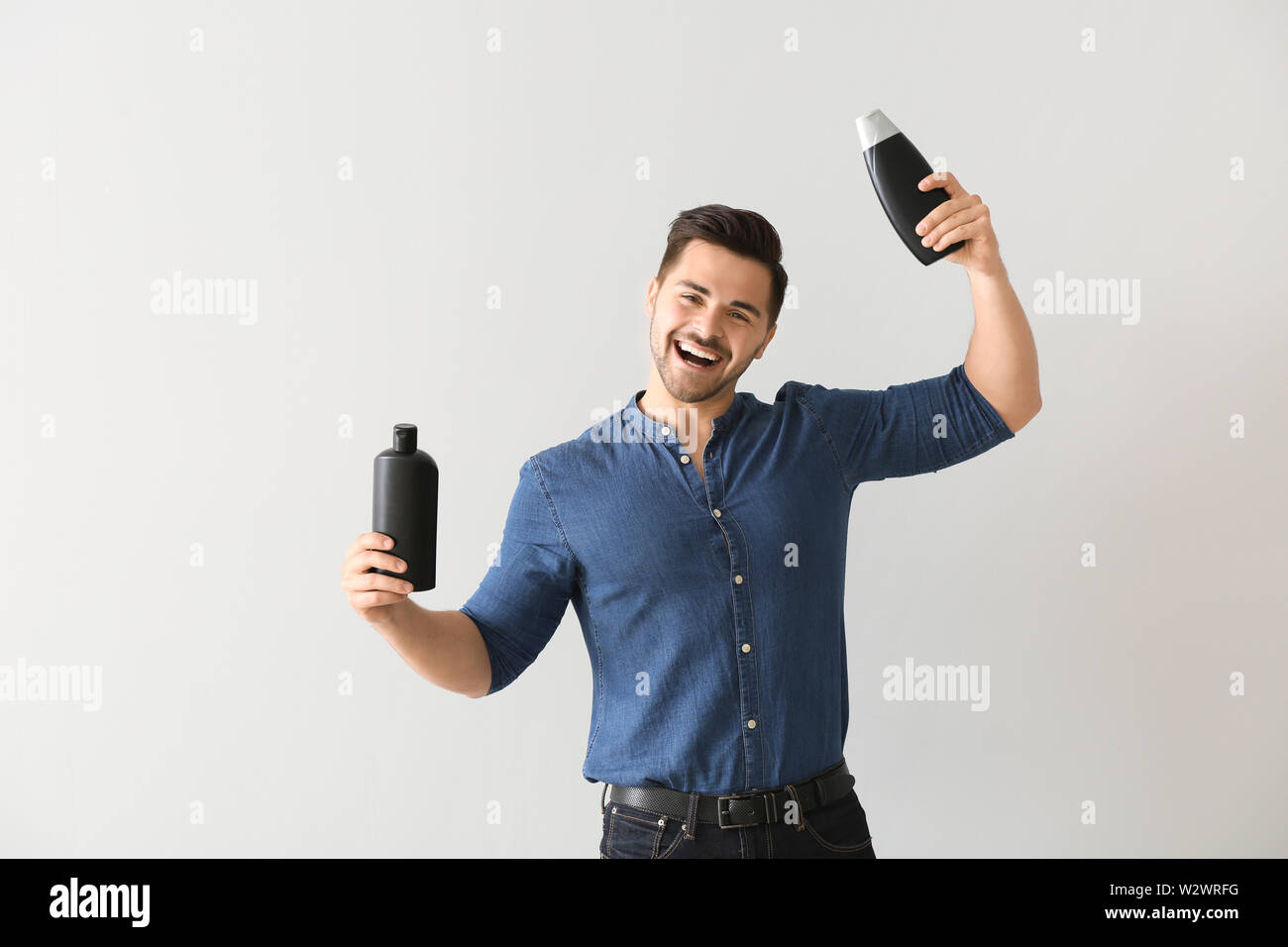 Handsome man with bottles of shampoo on light background Stock Photo ...