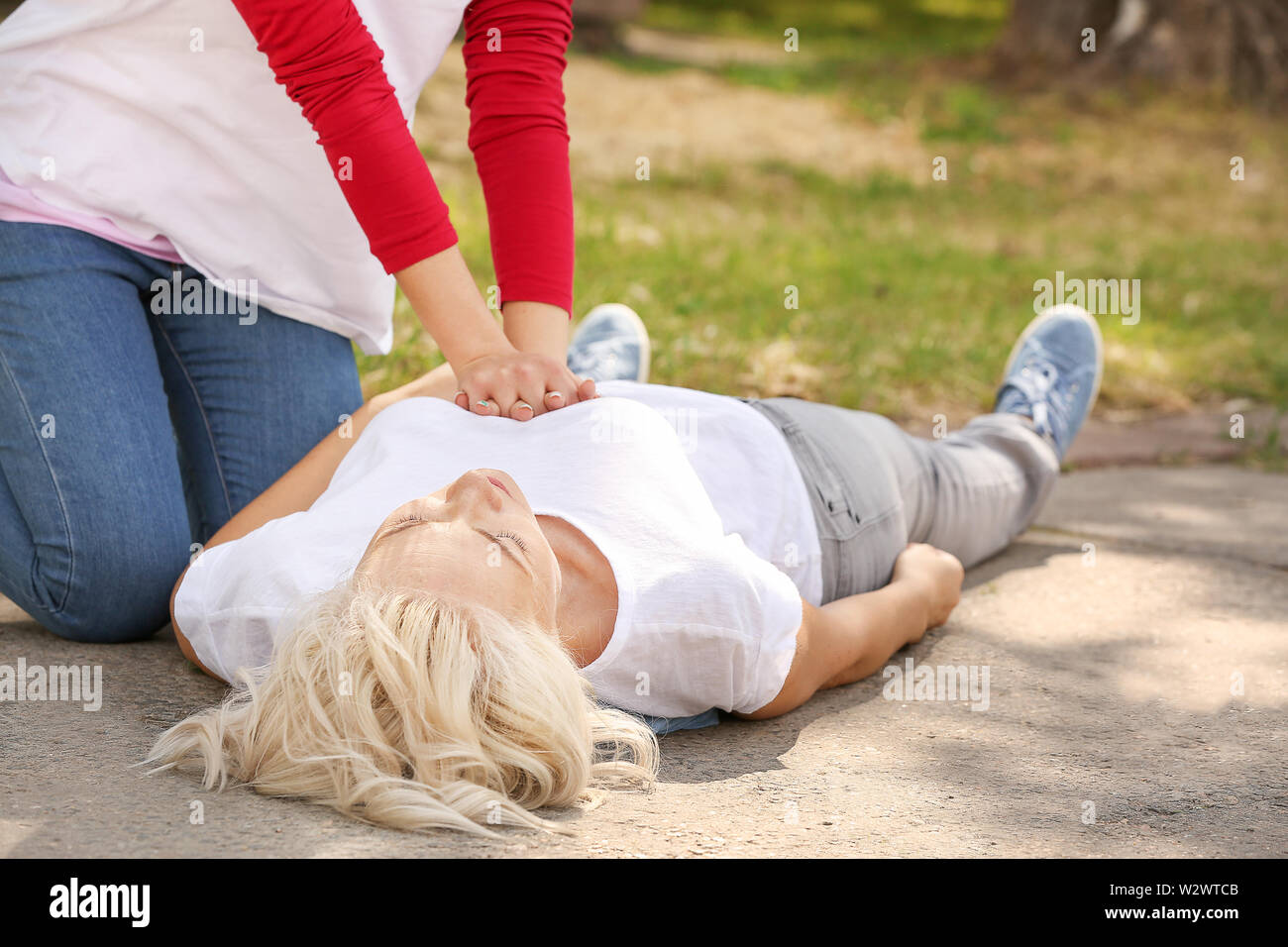 Female passer-by doing CPR on unconscious mature woman outdoors Stock ...