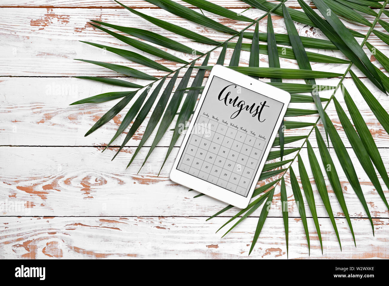 Tablet computer with calendar on screen and tropical leaves on wooden ...