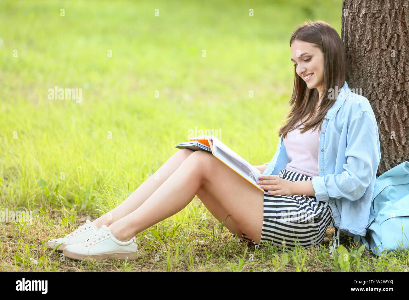 Beautiful female student sitting under tree in park Stock Photo - Alamy