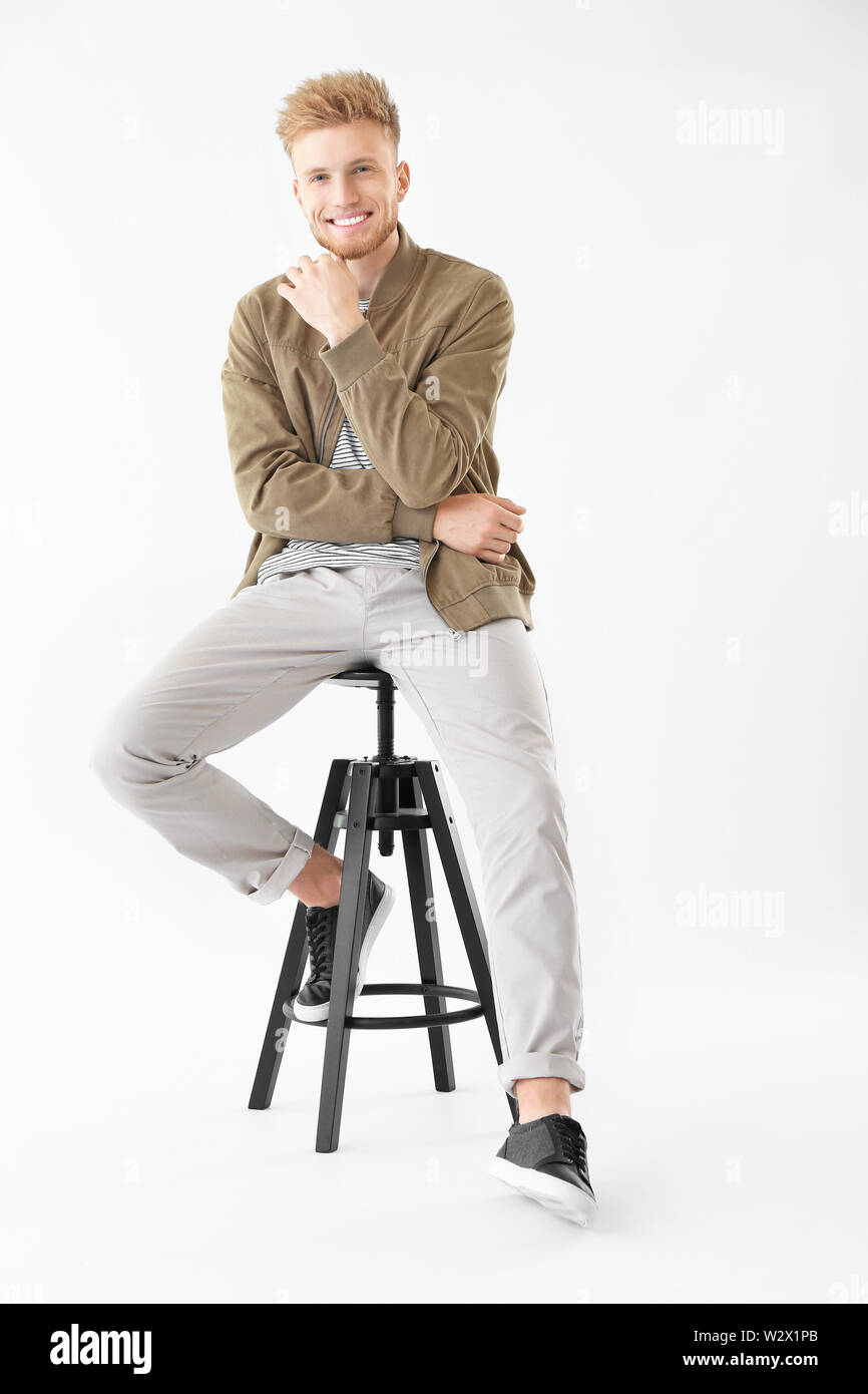 Stylish young man sitting on stool against white background Stock Photo ...
