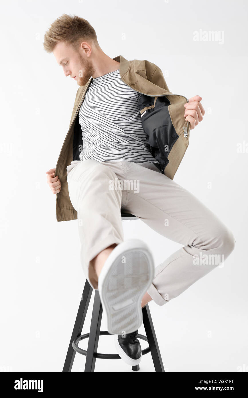 Stylish young man sitting on stool against white background Stock Photo ...