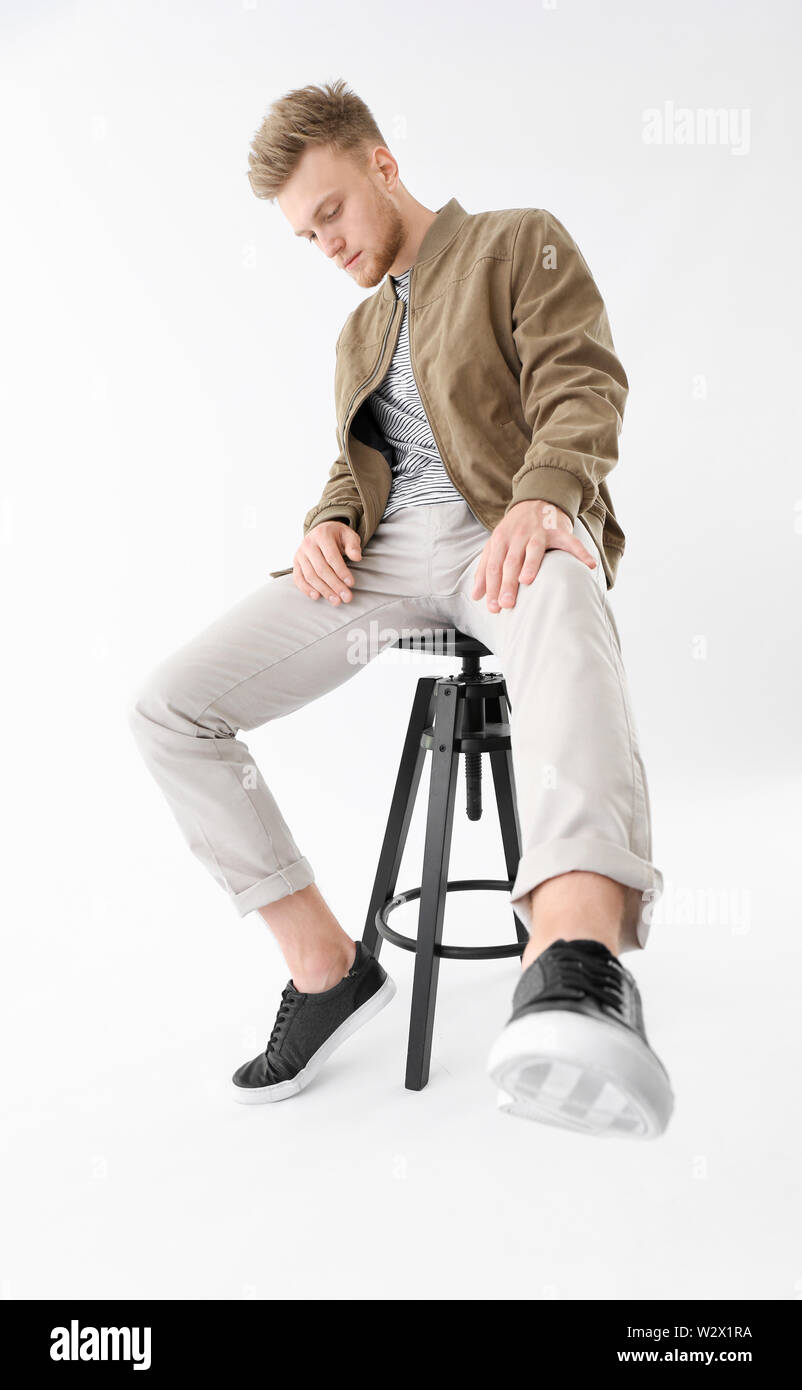 Stylish young man sitting on stool against white background Stock Photo ...