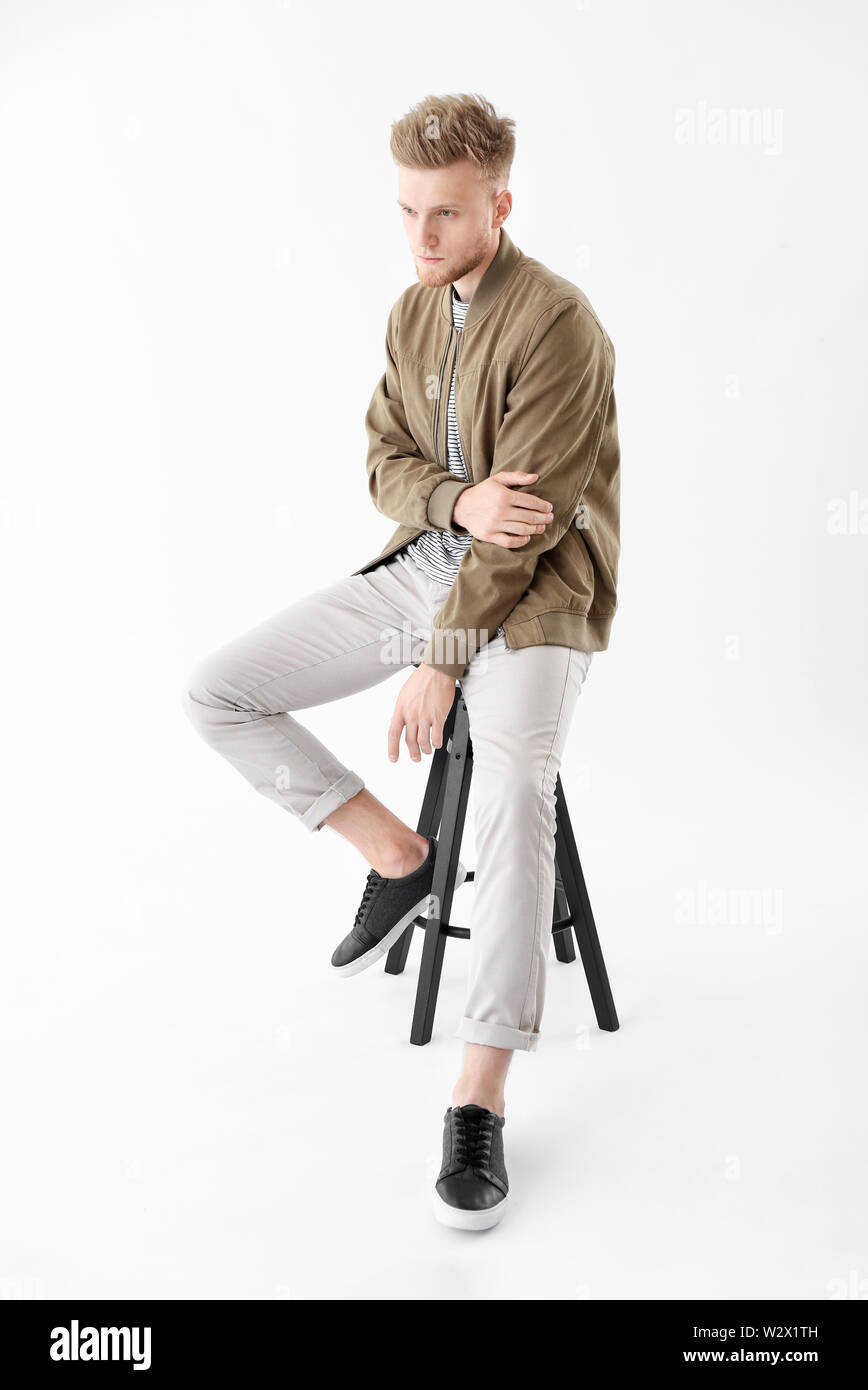 Stylish young man sitting on stool against white background Stock Photo ...