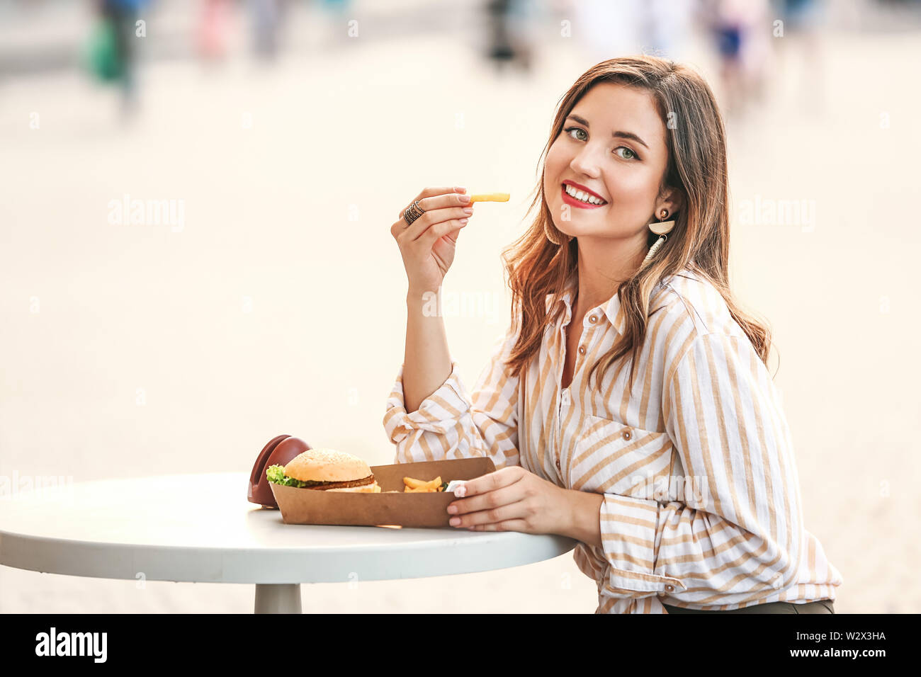 Beautiful young woman eating tasty french fries in outdoor cafe Stock ...
