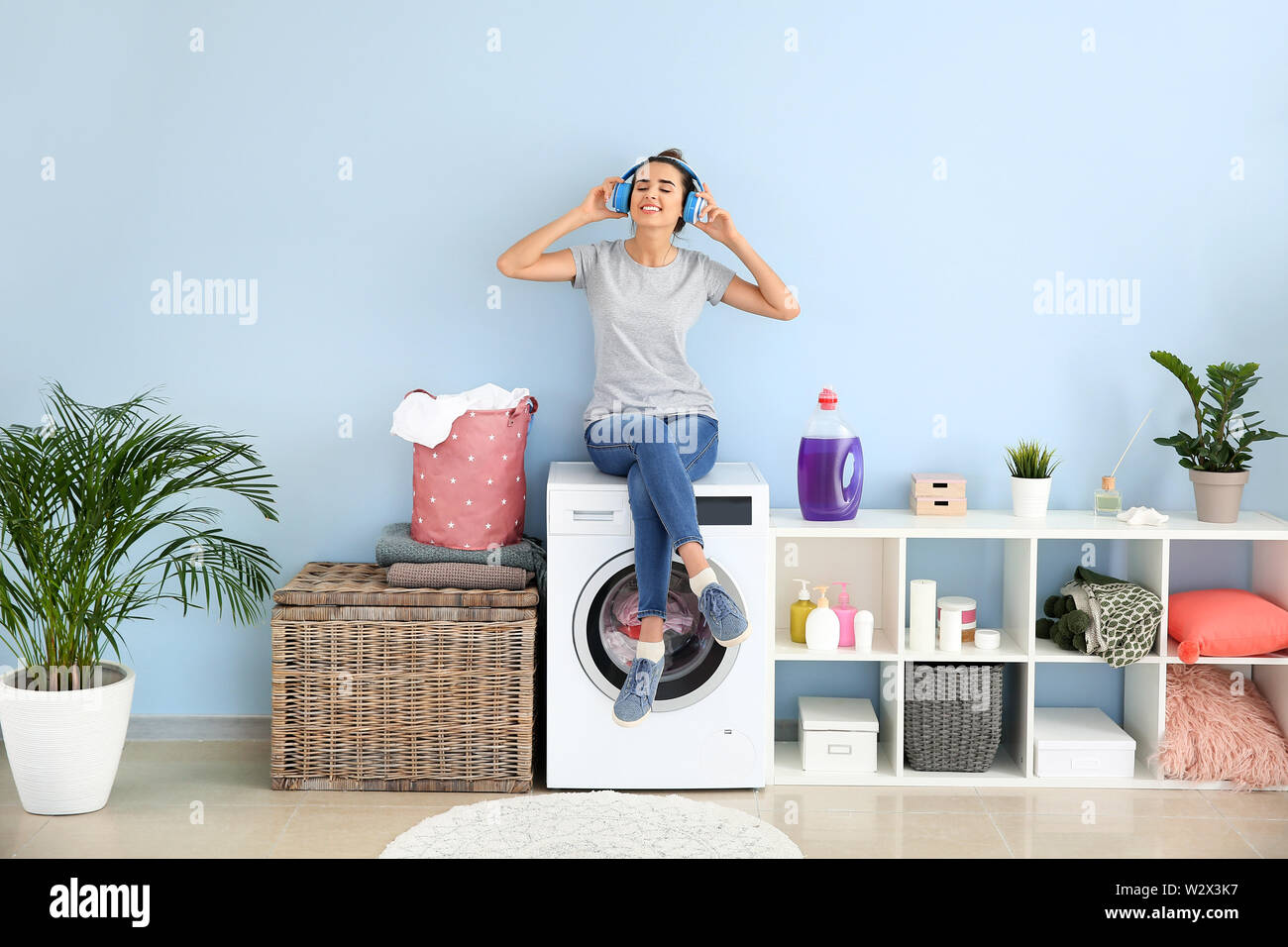 Beautiful young woman listening to music while doing laundry at home ...