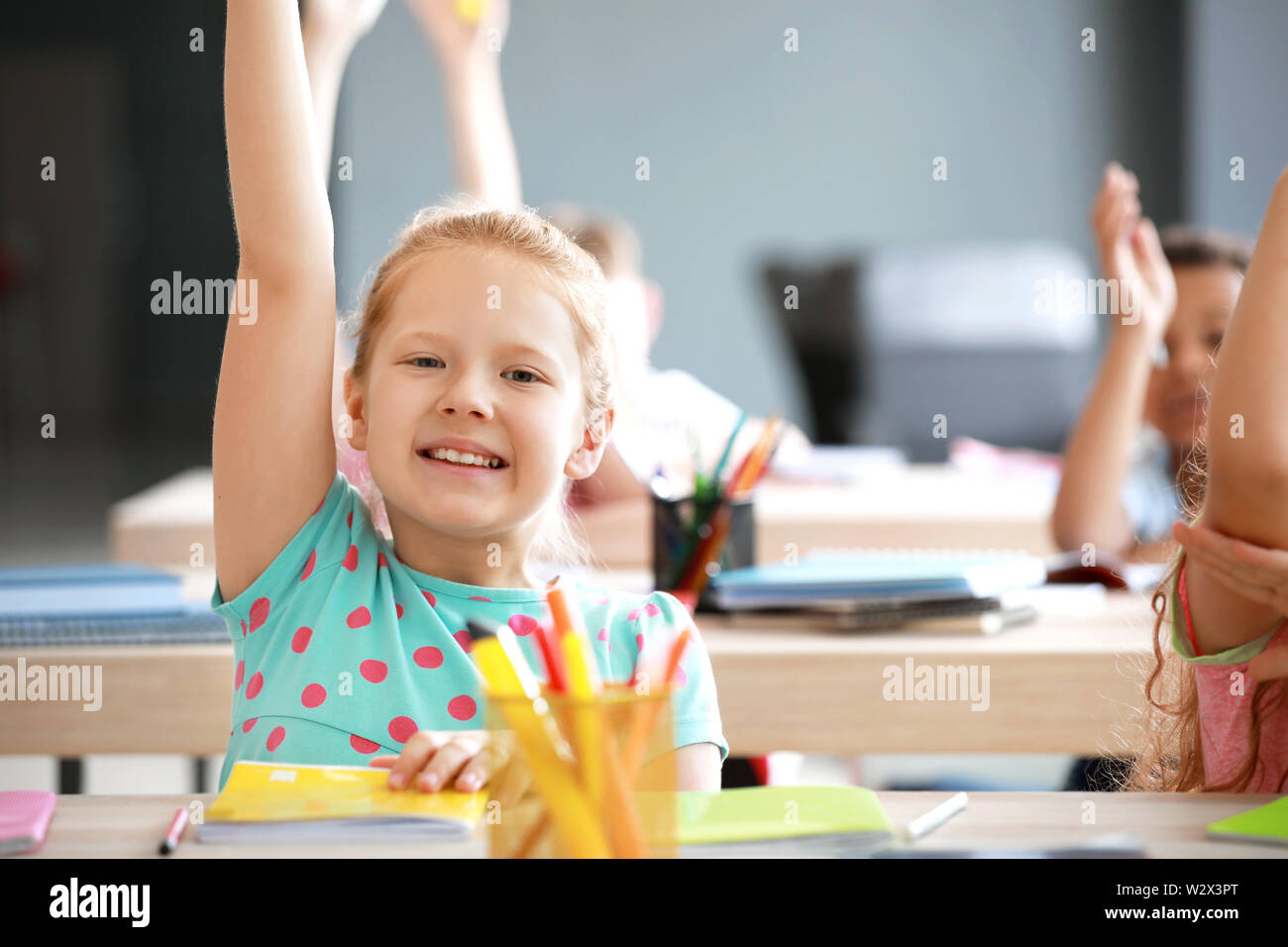 Cute little girl raising hand during lesson in classroom Stock Photo ...