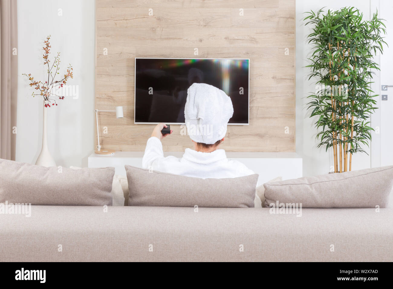Woman with remote control sitting on couch with towel on her head ...