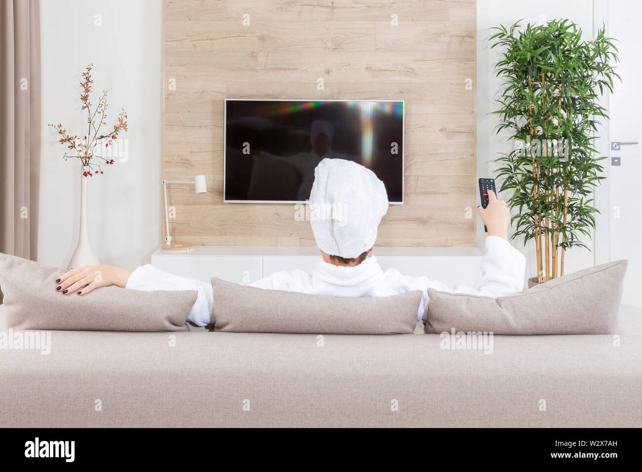 Woman with remote control sitting on couch with towel on her head ...