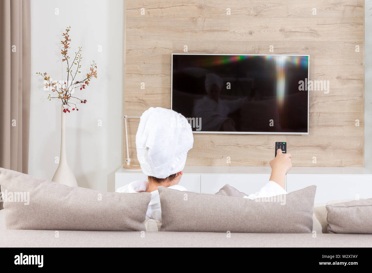 Woman with remote control sitting on couch with towel on her head ...