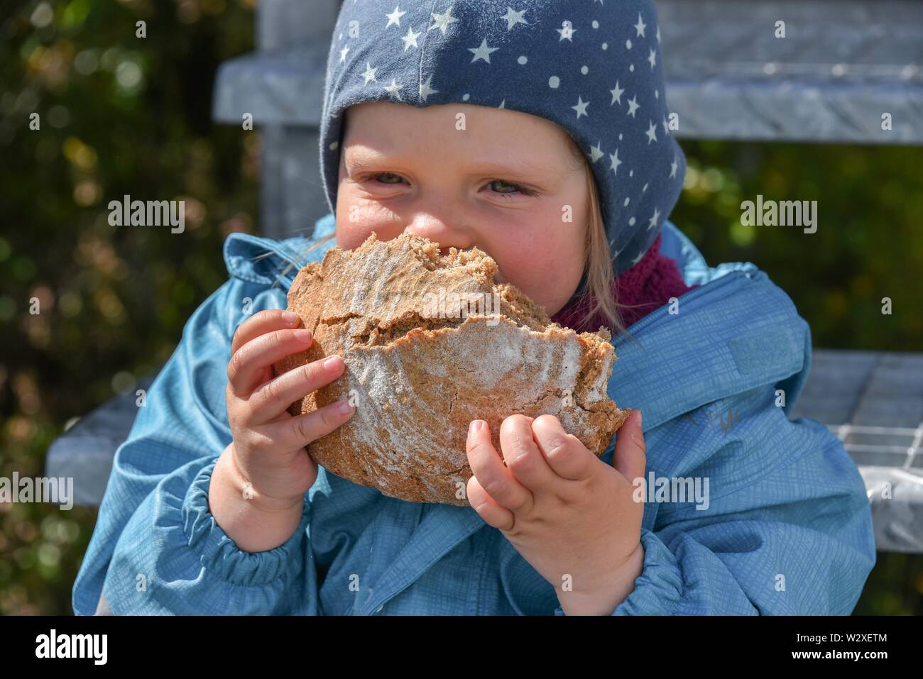 Little girl biting heartily into a black bread hi-res stock photography ...