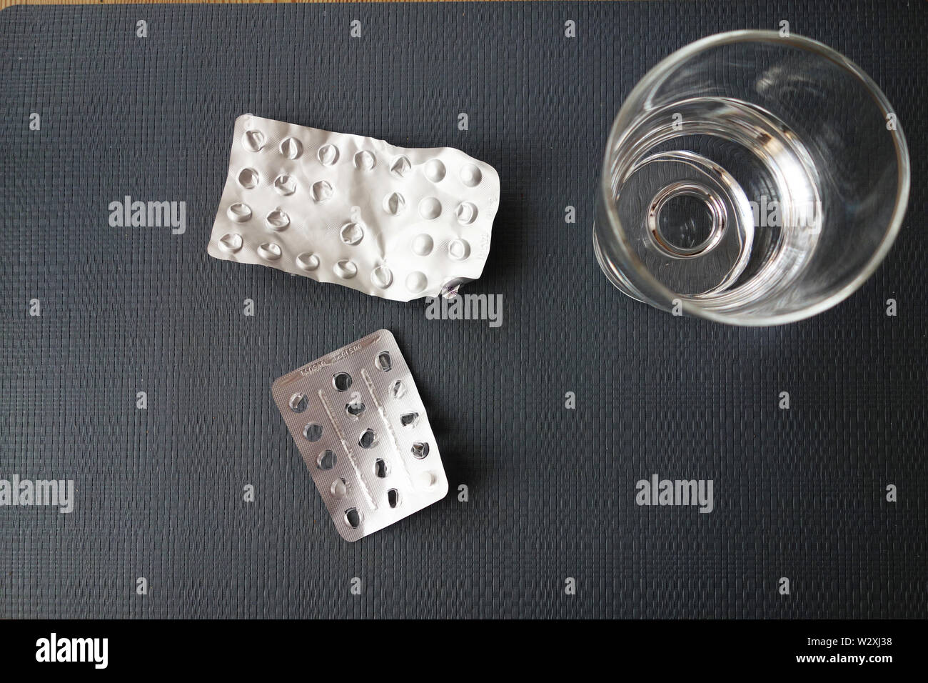 two Blisters of medications and a glass of water on grey background ...