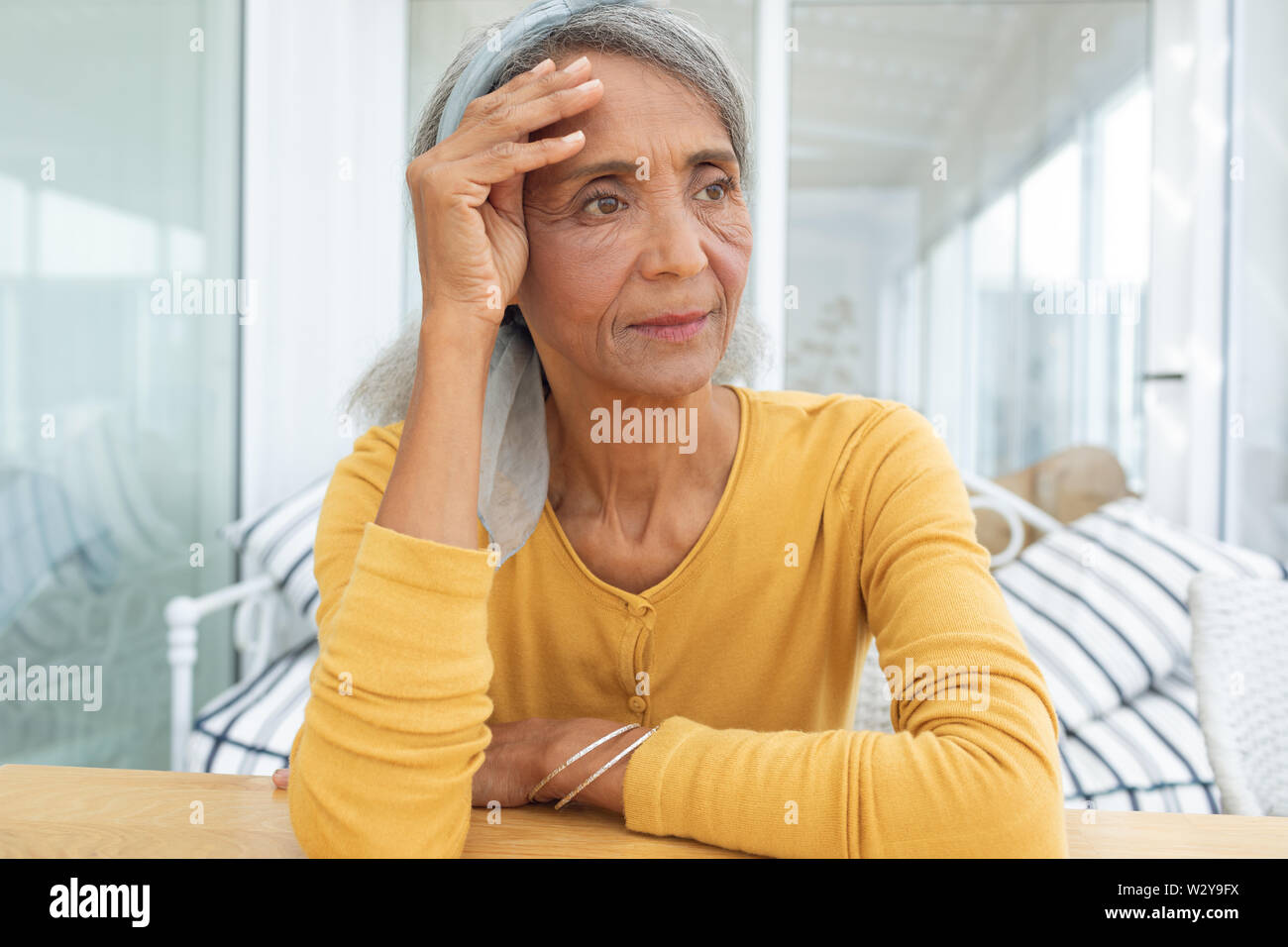 Woman inside a room with arms over table and hand on the forehead Stock ...