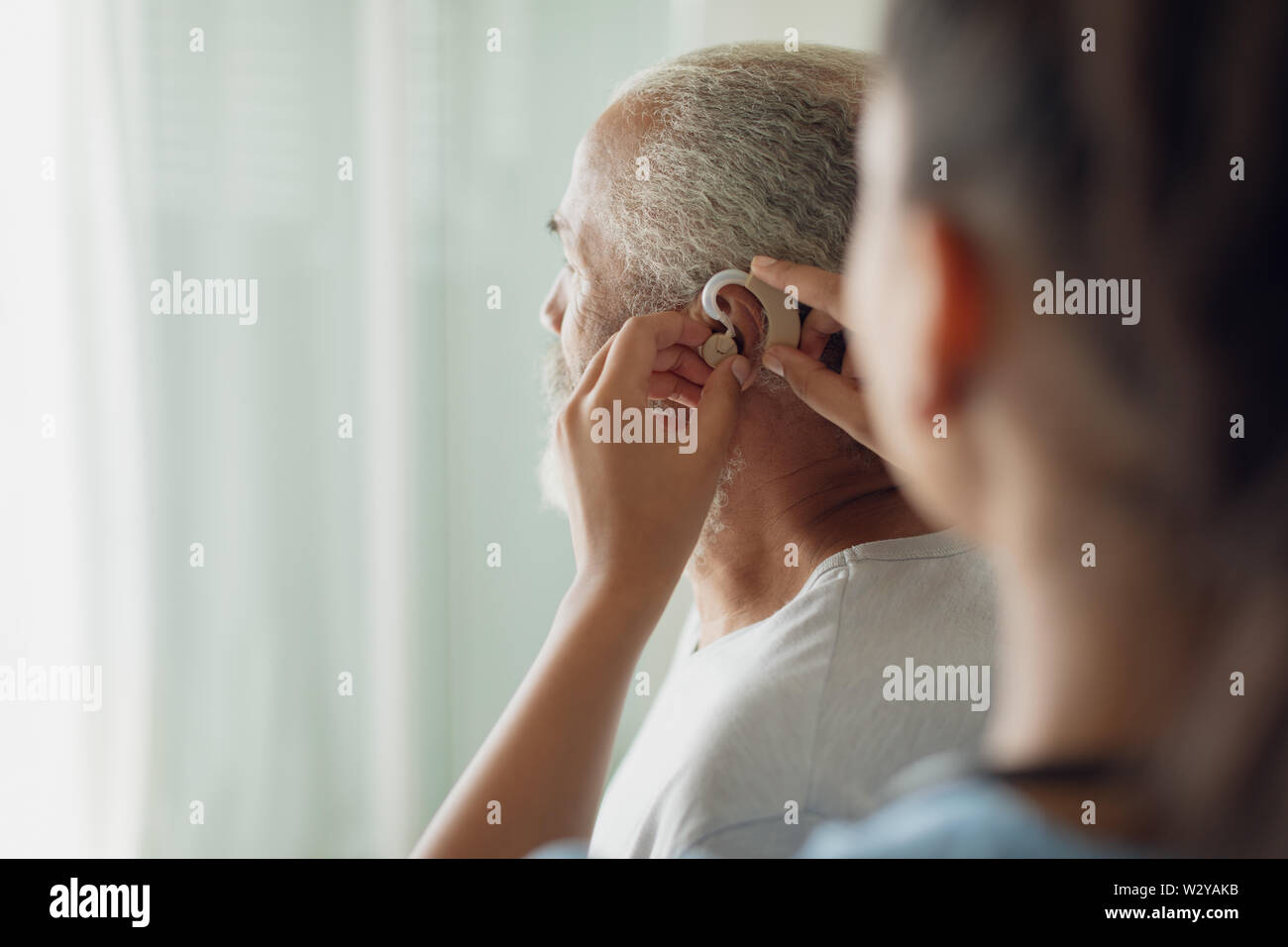 Healthcare worker putting hearing aid Stock Photo - Alamy