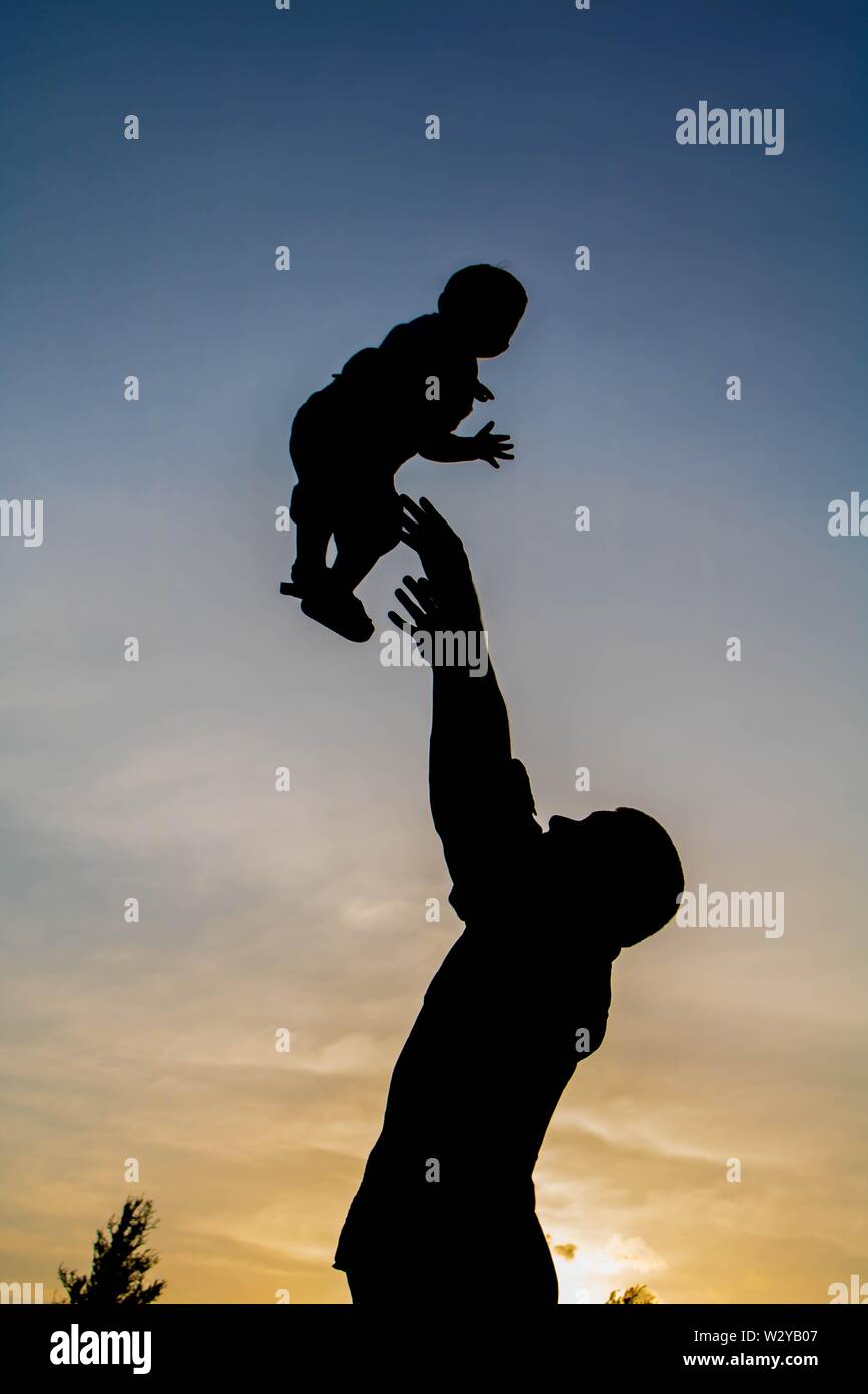 Silhouette of a father and his baby playing together with clouds and ...