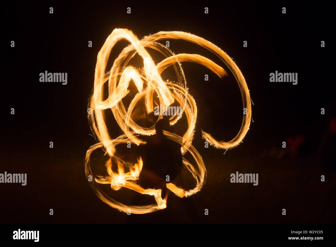 An artist shows a fire show at night spinning torches, circles of fire ...