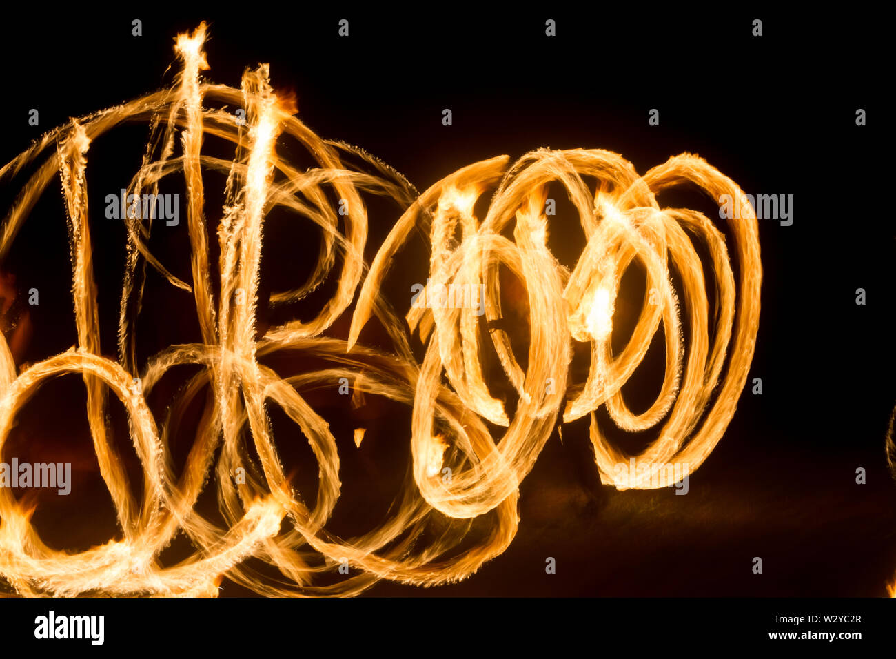 An artist shows a fire show at night spinning torches, circles of fire ...