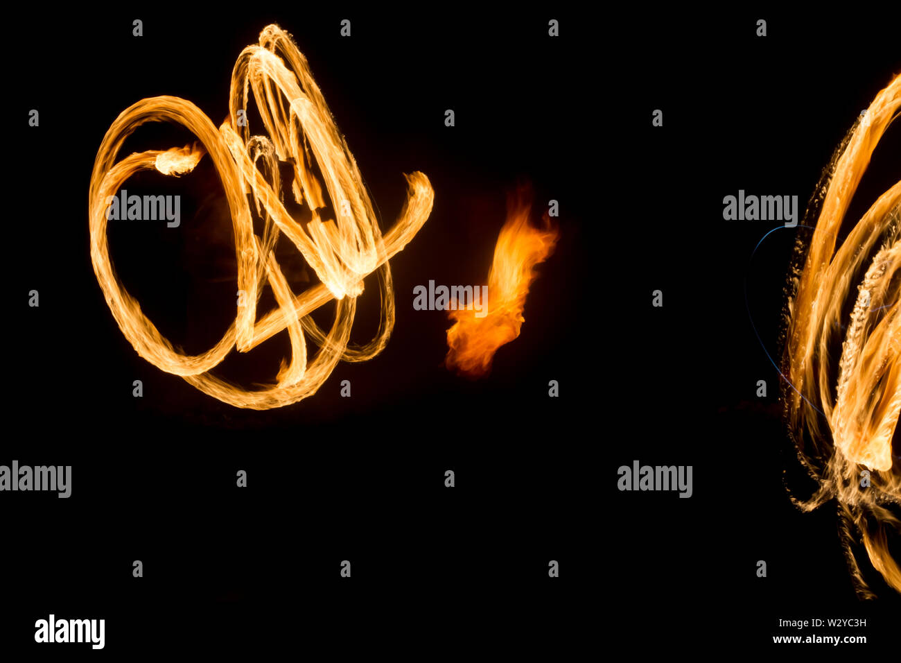 An artist shows a fire show at night spinning torches, circles of fire ...